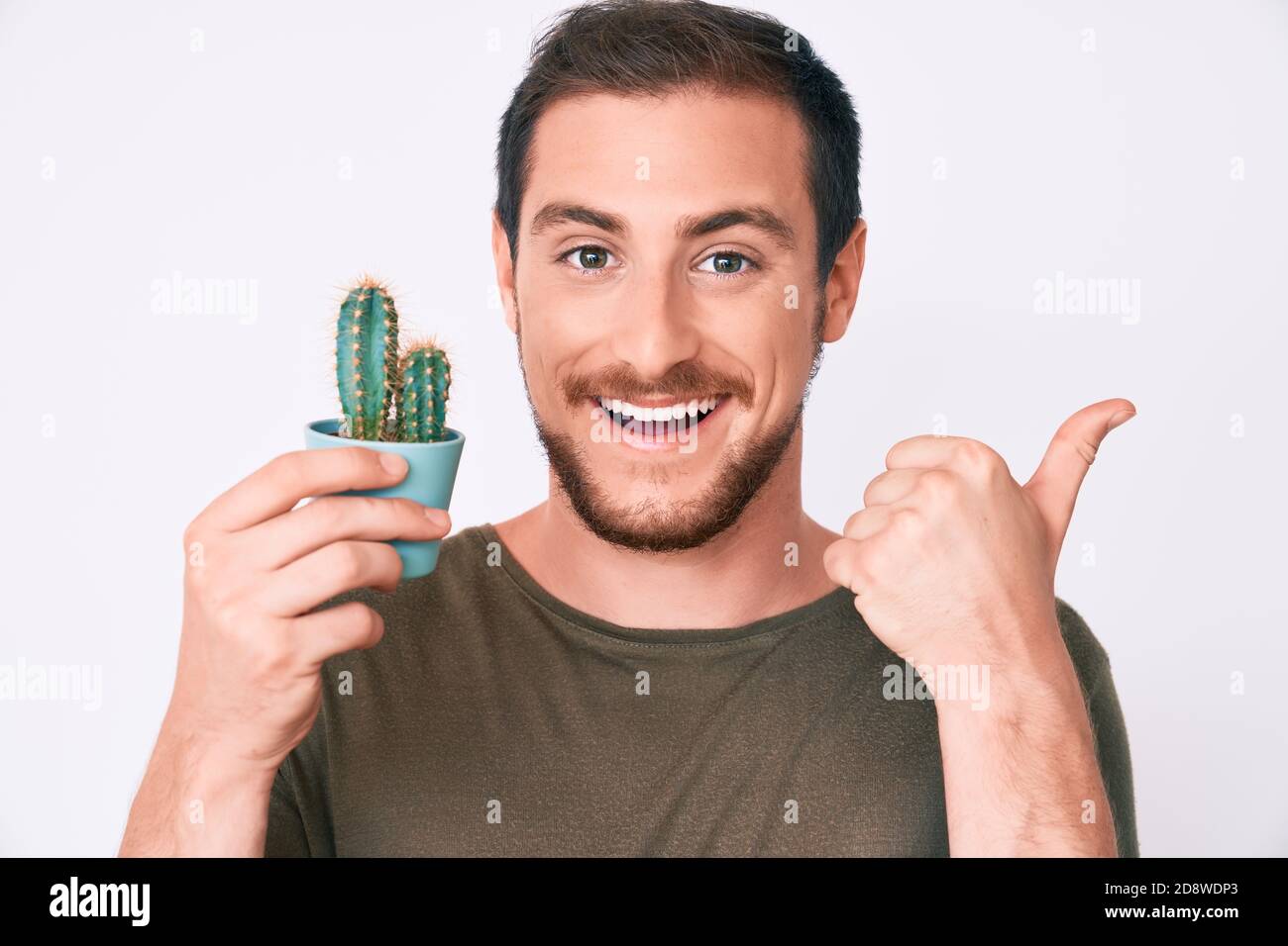 Young handsome man holding small cactus pot pointing thumb up to the ...
