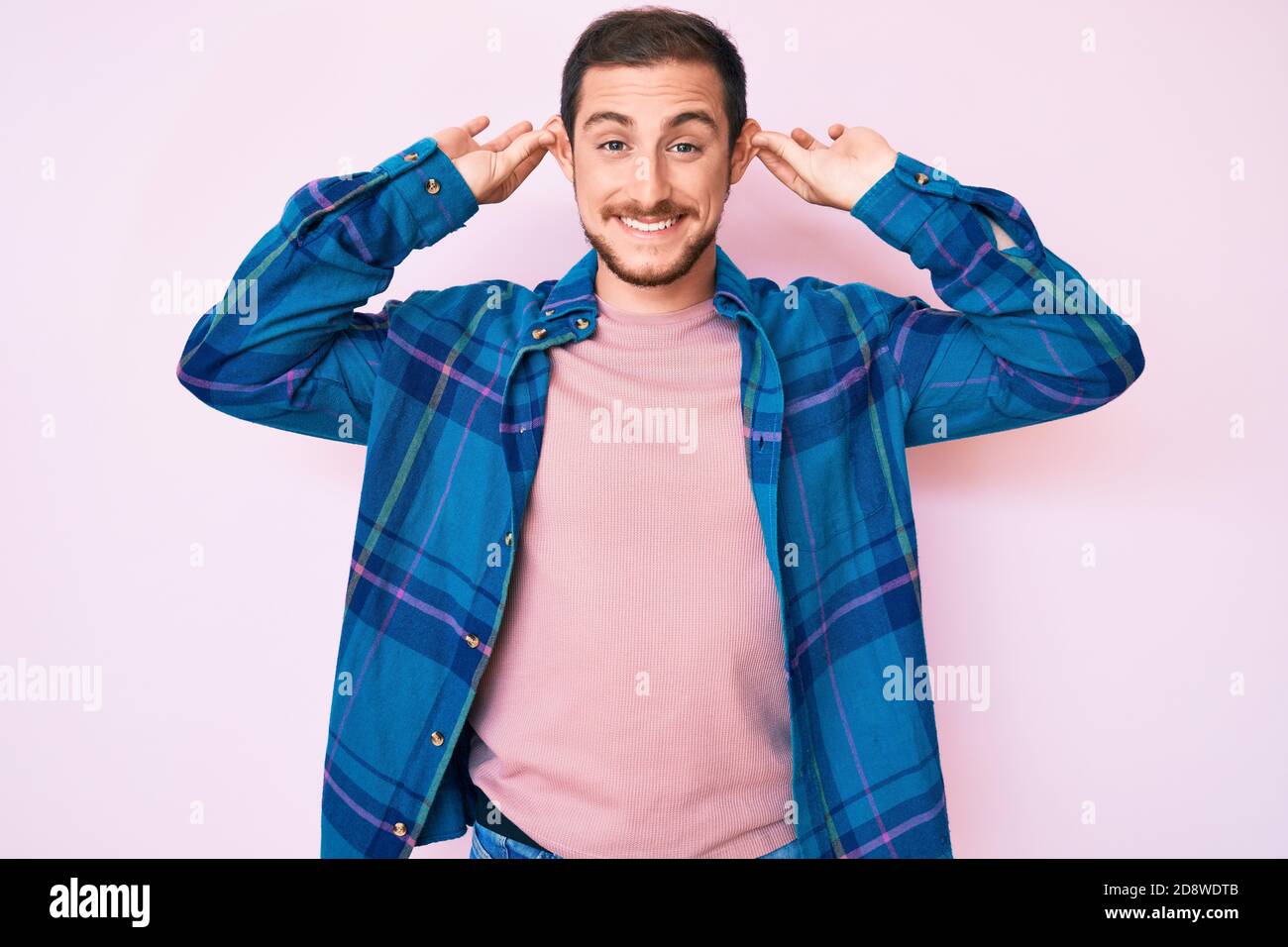 Young handsome man wearing casual clothes smiling pulling ears with ...