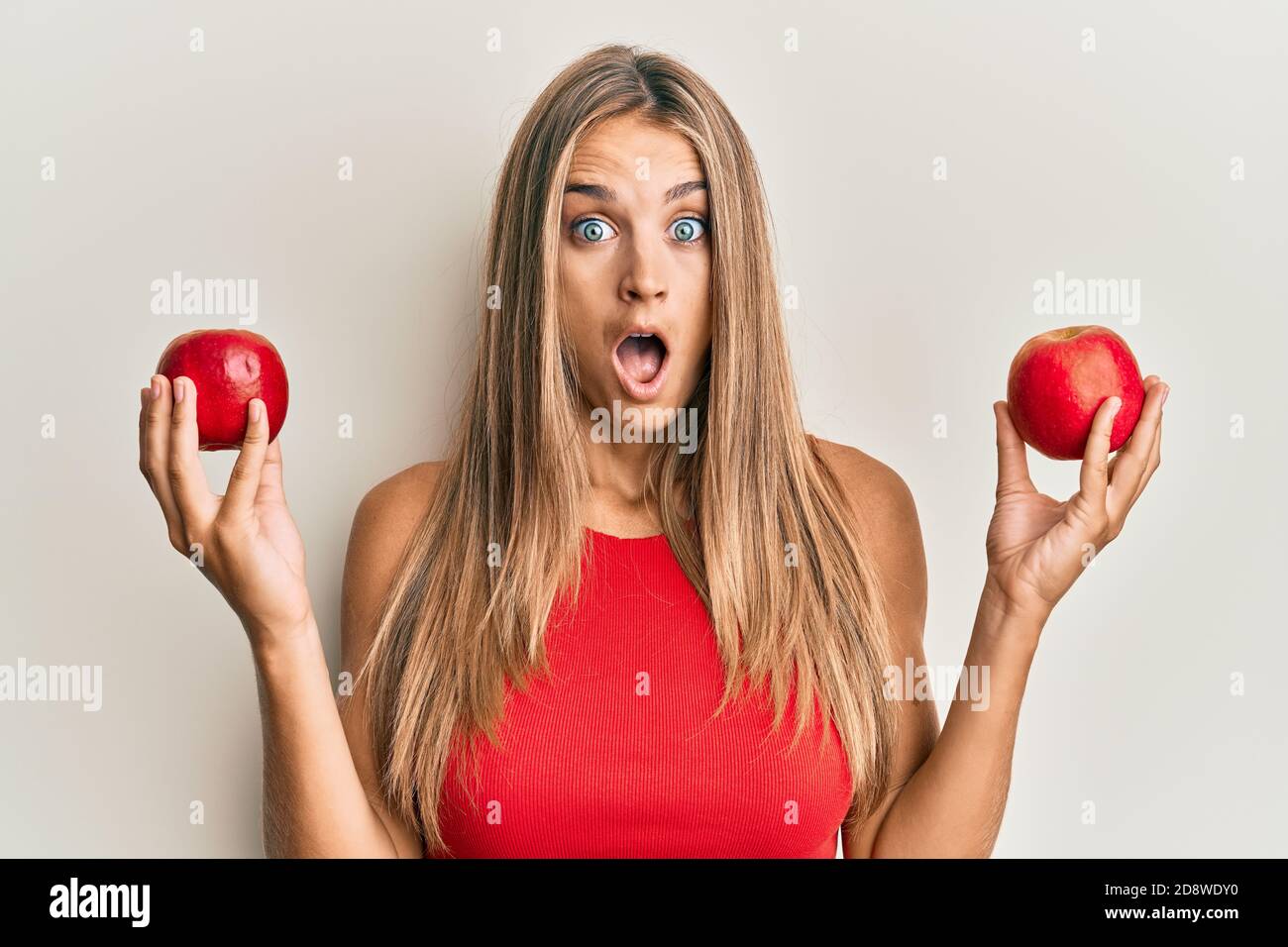 Young blonde woman holding red apples afraid and shocked with surprise ...