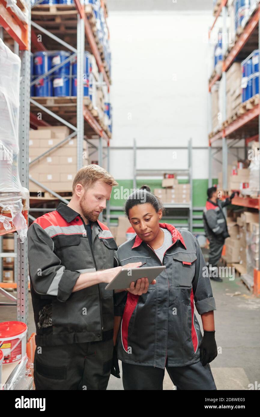 Young foreman showing his mixed-race female colleague list of new goods ...