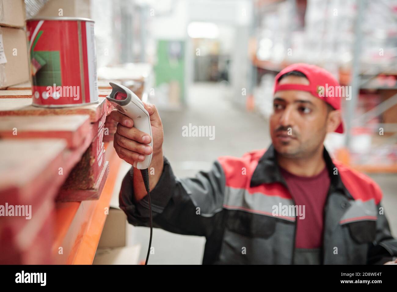 Worker of contemporary large warehouse scanning qr code of tin with ...