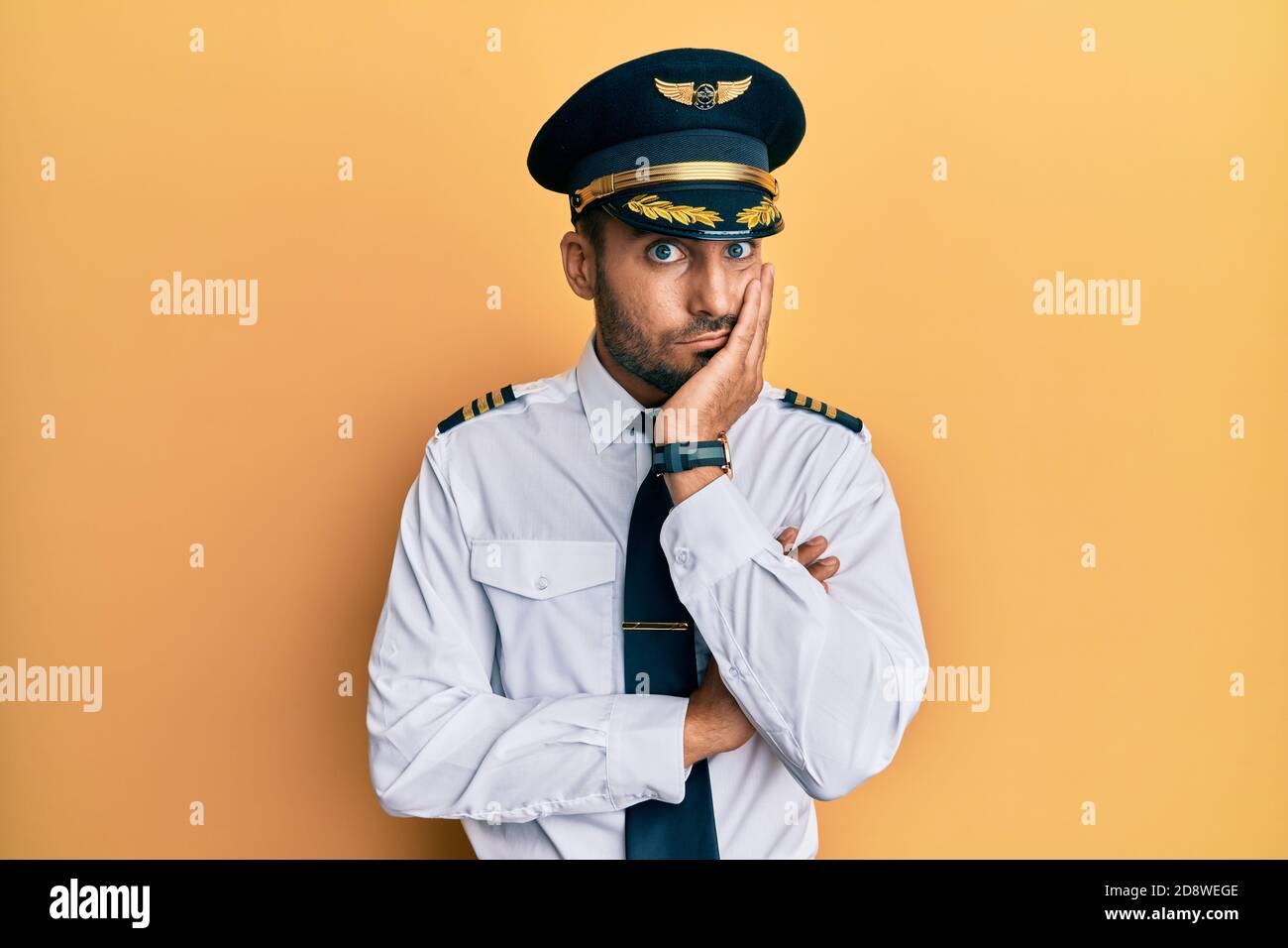 Handsome hispanic man wearing airplane pilot uniform thinking looking ...