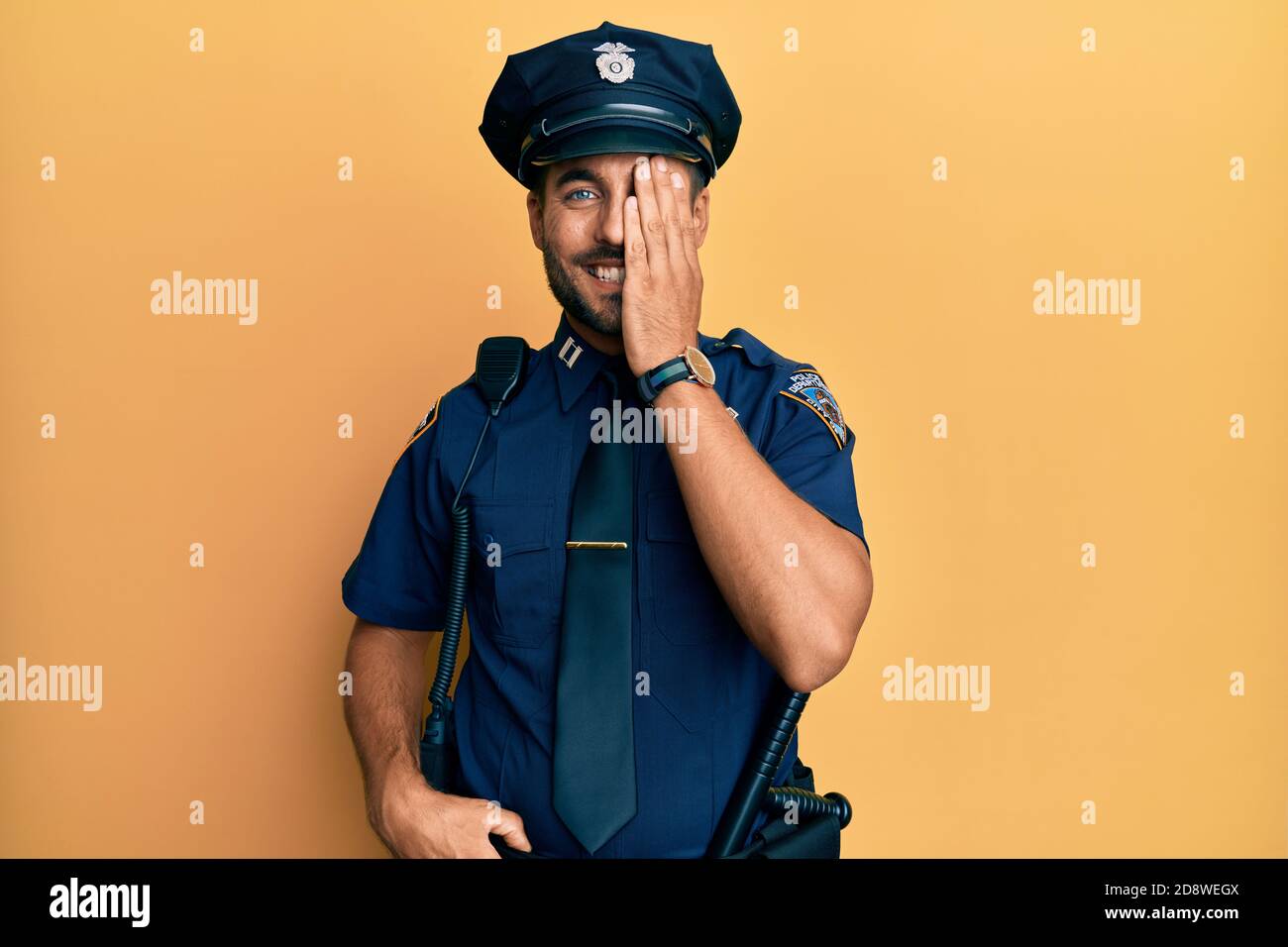 Handsome hispanic man wearing police uniform covering one eye with hand ...