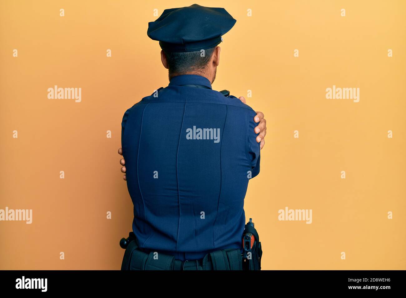 Handsome hispanic man wearing police uniform hugging oneself happy and ...