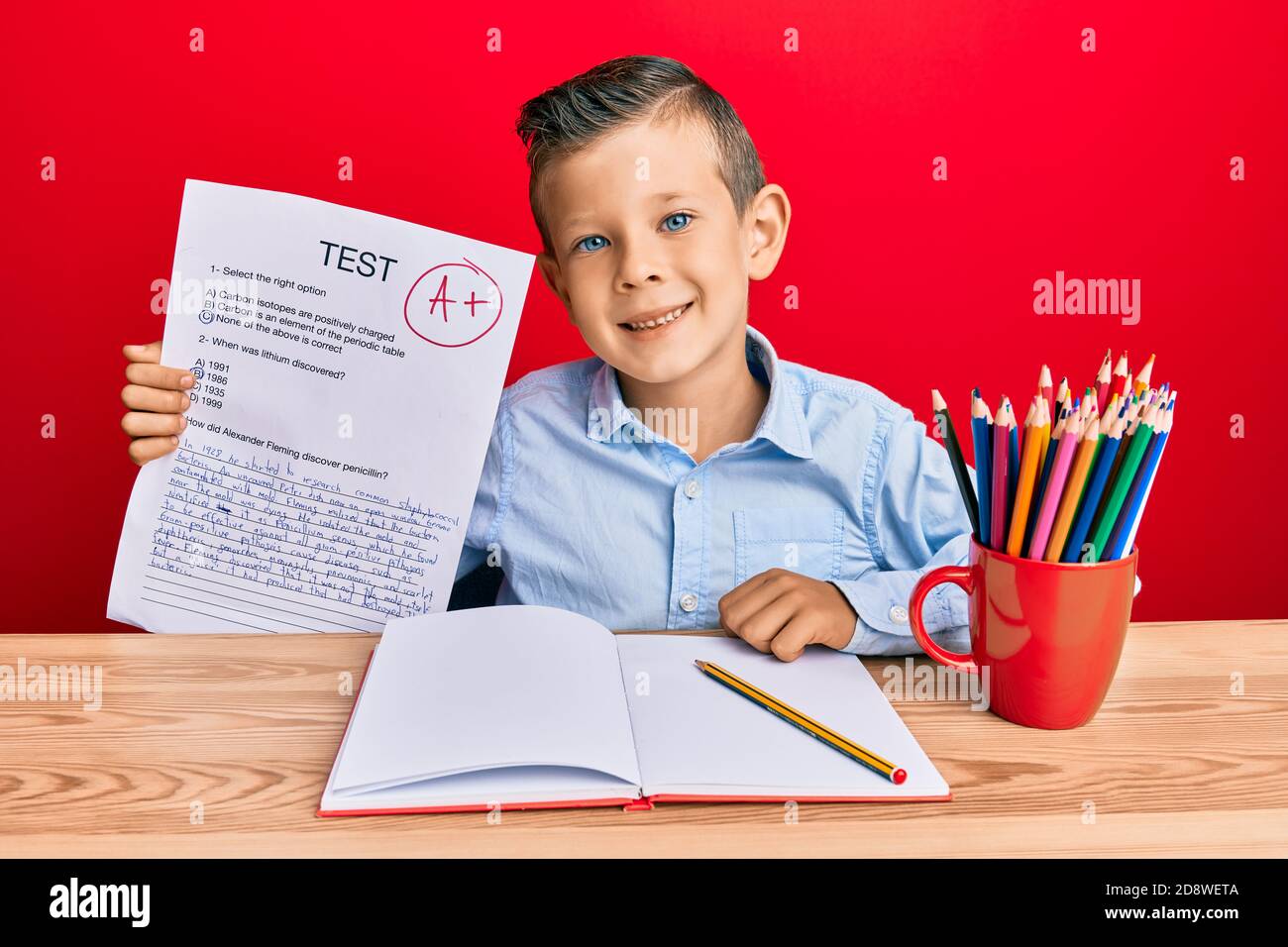 Adorable caucasian kid holding passed test sitting on the table looking ...