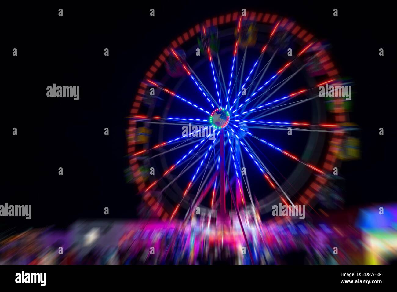 Radial blur of a ferris wheel at night. The ferris wheel is lit up red ...