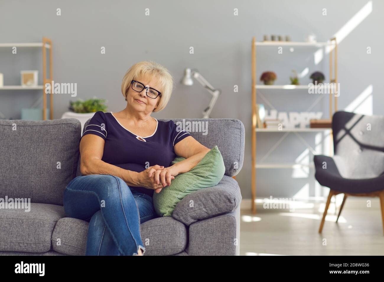Mature woman sitting on comfortable sofa in her modern living-room and ... Mature woman sitting on comfortable sofa in her modern living-room and ...