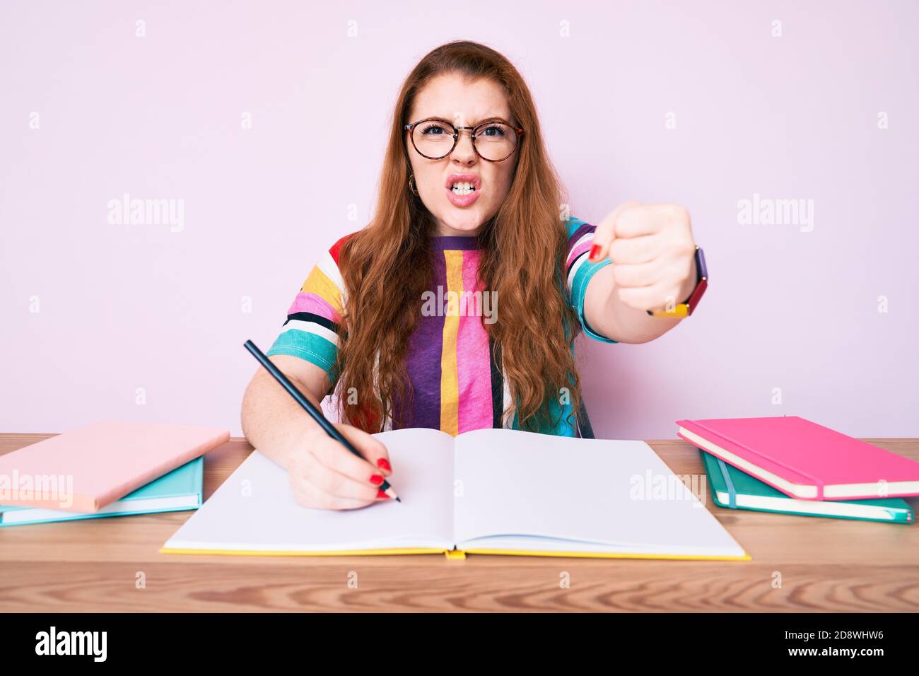Young redhead woman sitting on the table writing book annoyed and ...