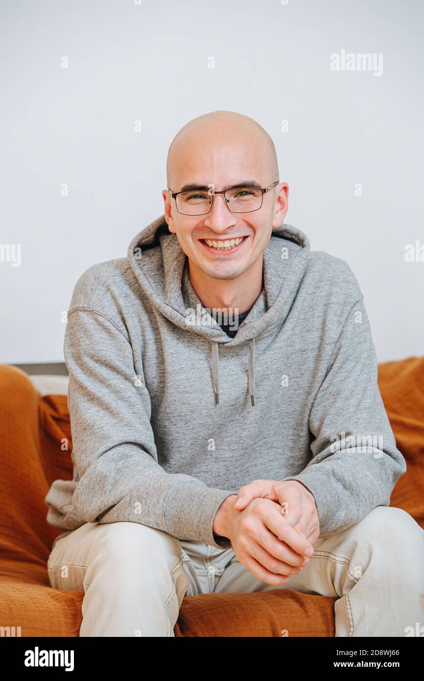 Portrait of a happy smiling happy bold man in glasses sitting on a sofa ...