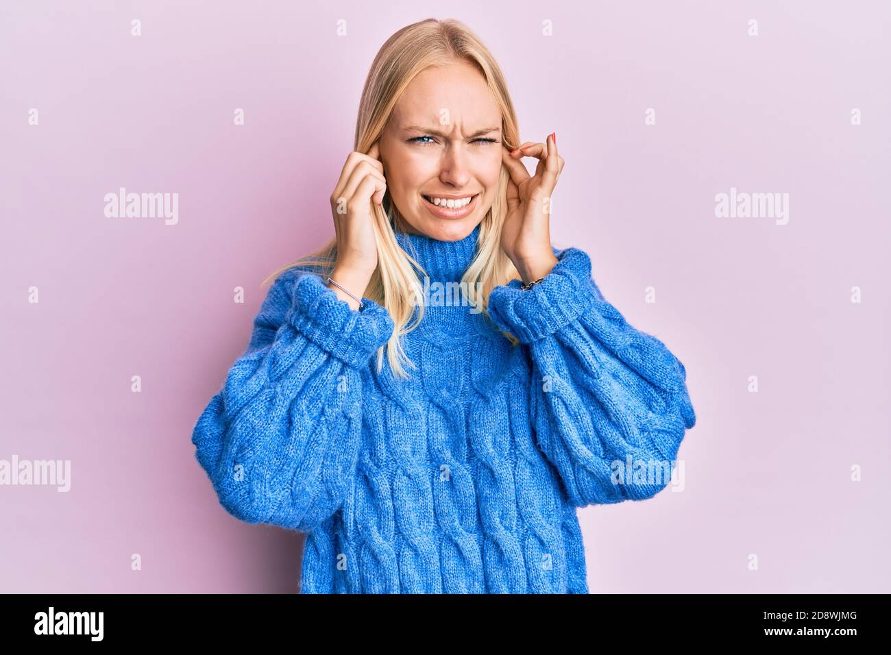 Young blonde girl wearing wool winter sweater covering ears with ...
