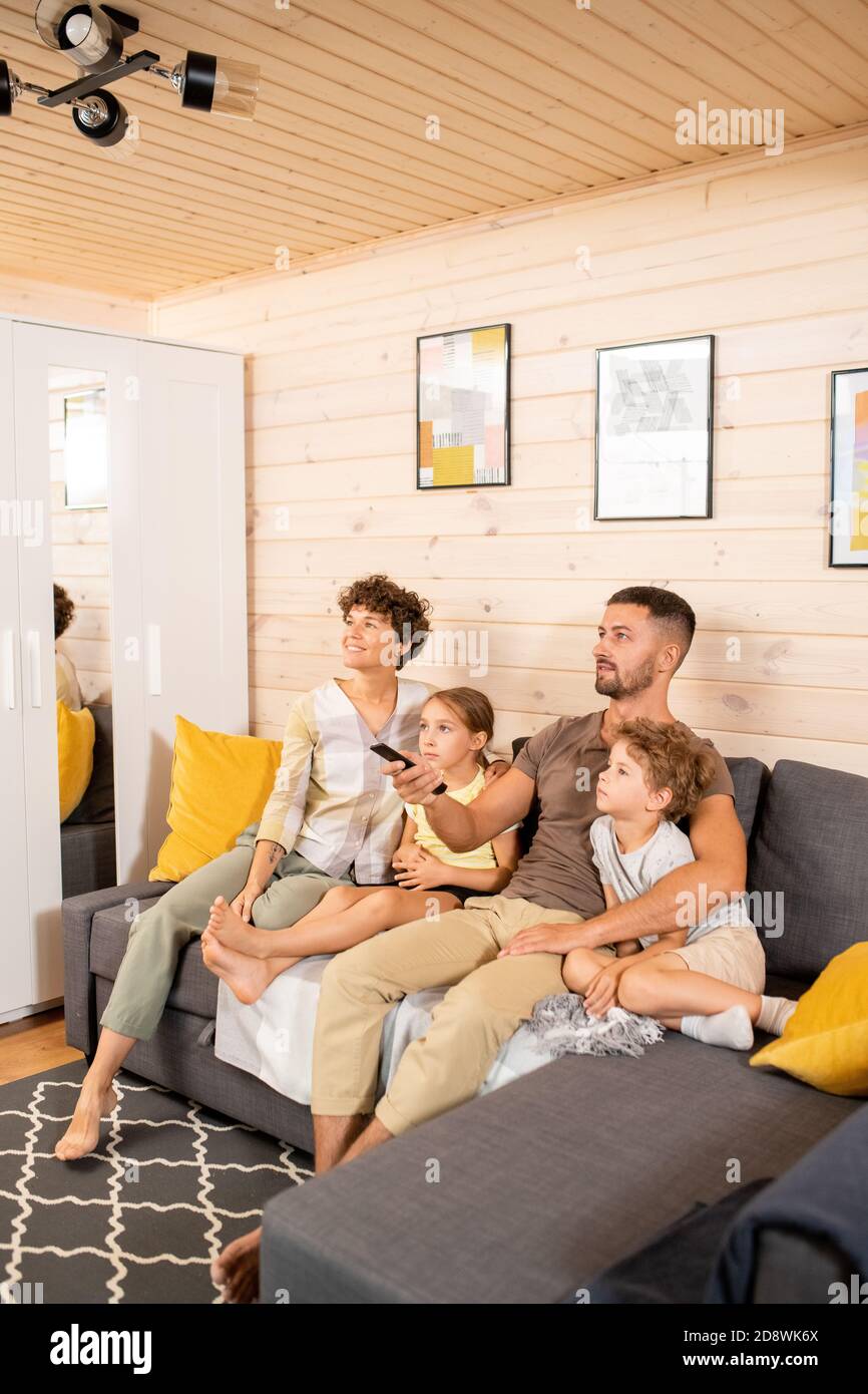 Young contemporary couple and their two cute little kids watching tv ...