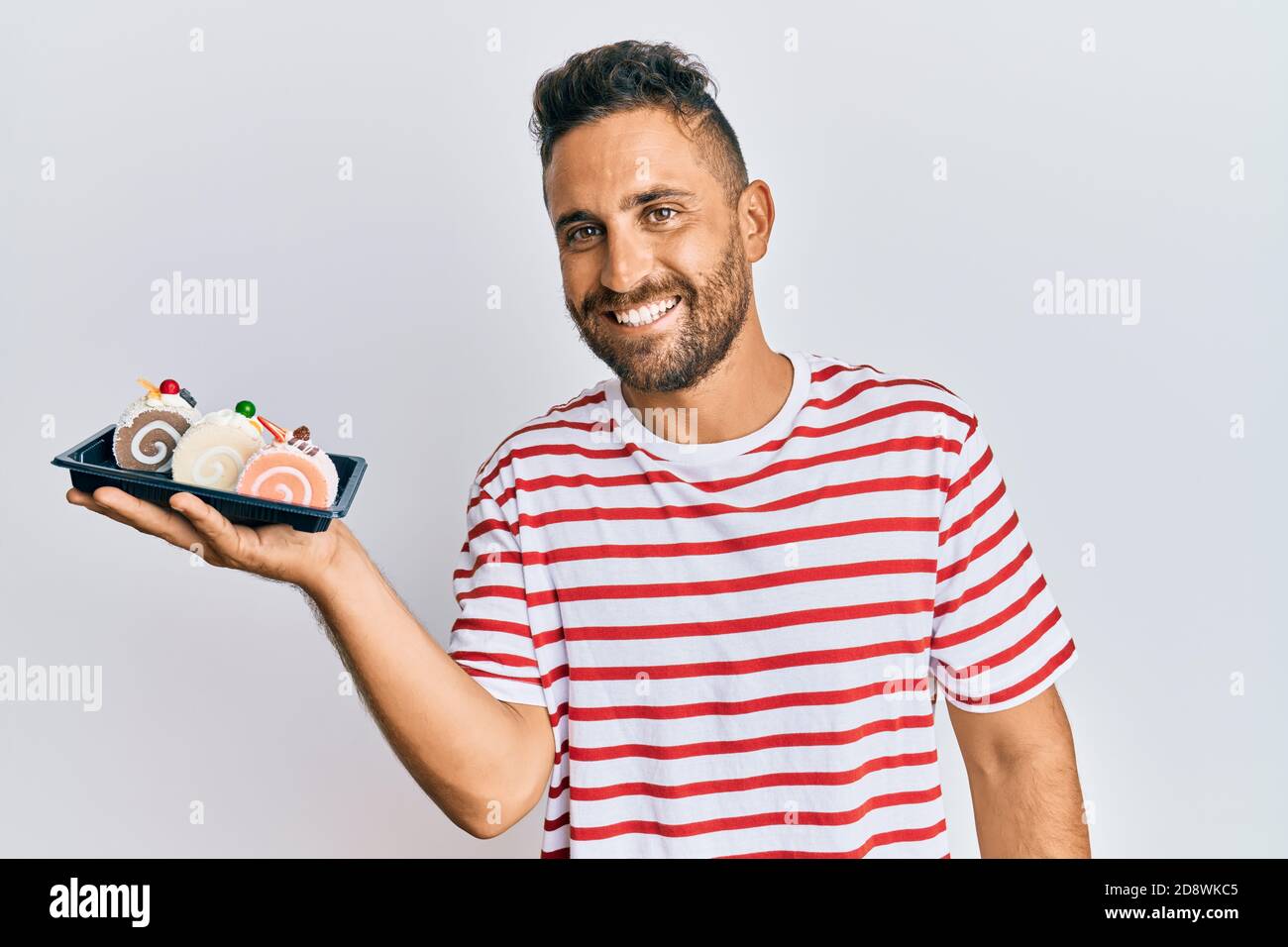 Handsome man with beard holding cake sweets looking positive and happy ...