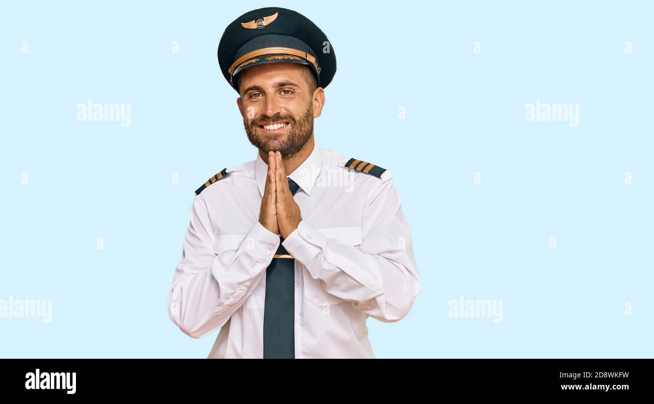 Handsome man with beard wearing airplane pilot uniform praying with ...