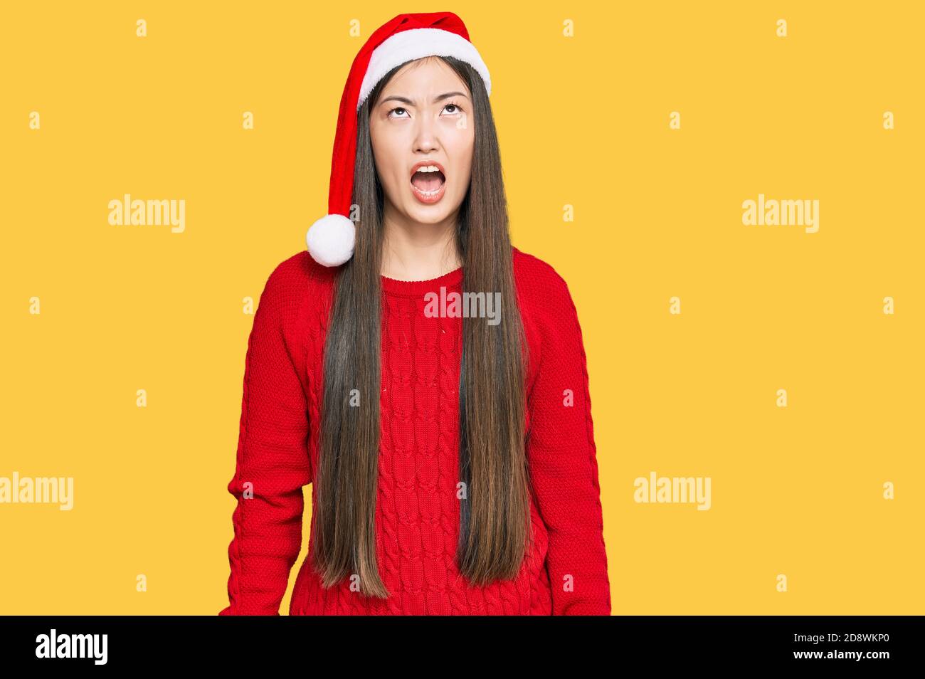 Young chinese woman wearing christmas hat angry and mad screaming ...