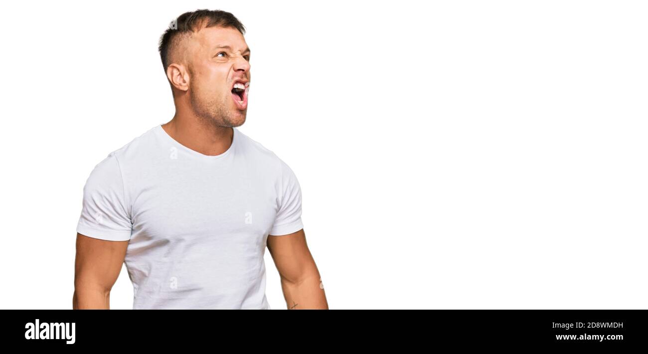 Handsome muscle man wearing casual white tshirt angry and mad screaming ...