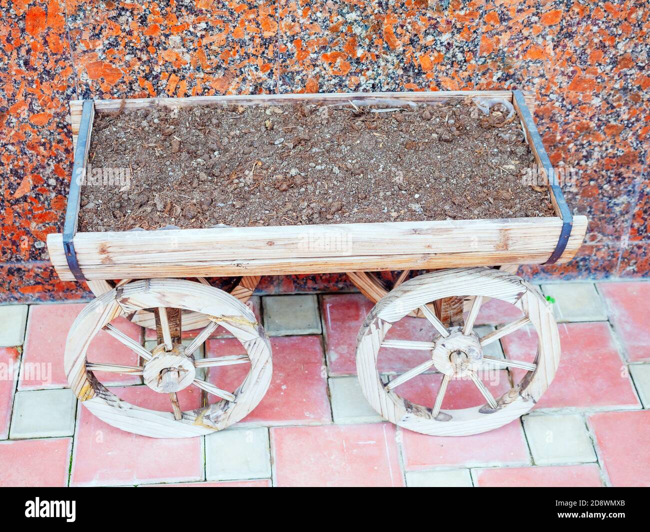 A decorative plant pot in the form of a wooden cart with soil stands ...