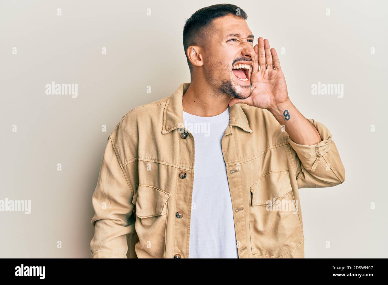 Handsome man with tattoos wearing casual brown denim jacket shouting ...