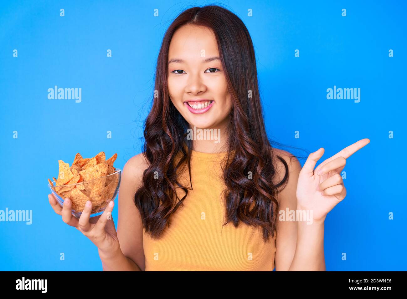 Young beautiful chinese girl holding nachos potato chips smiling happy ...