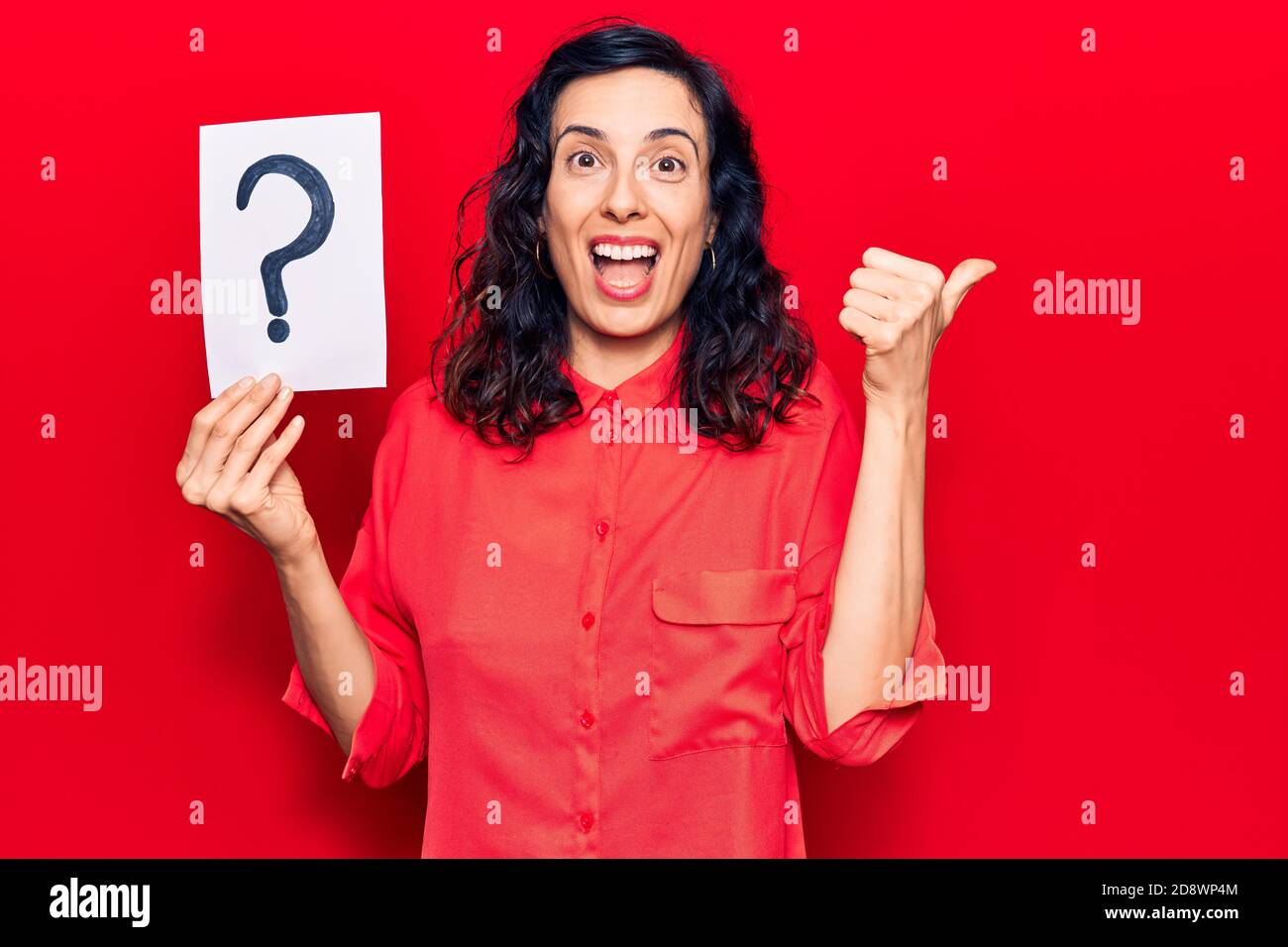 Young beautiful hispanic woman holding question mark pointing thumb up ...