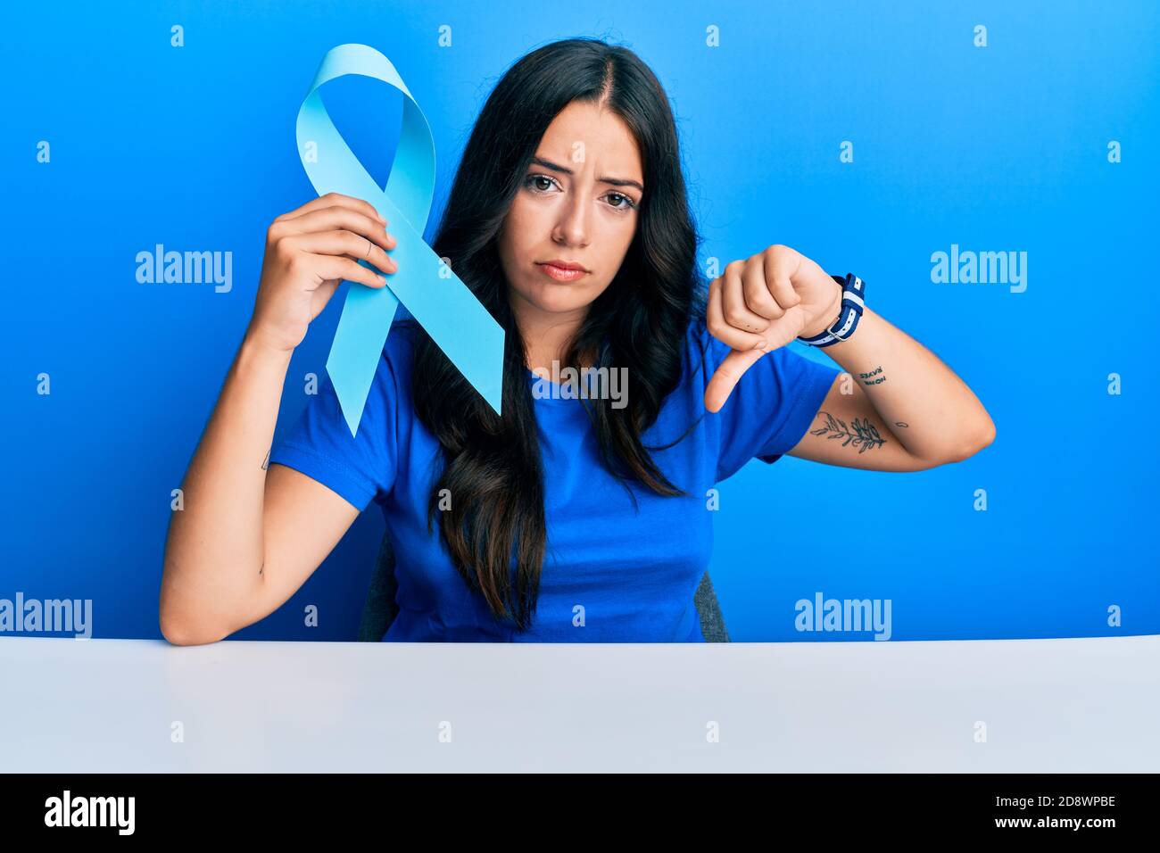 Beautiful brunette young woman holding blue ribbon with angry face ...