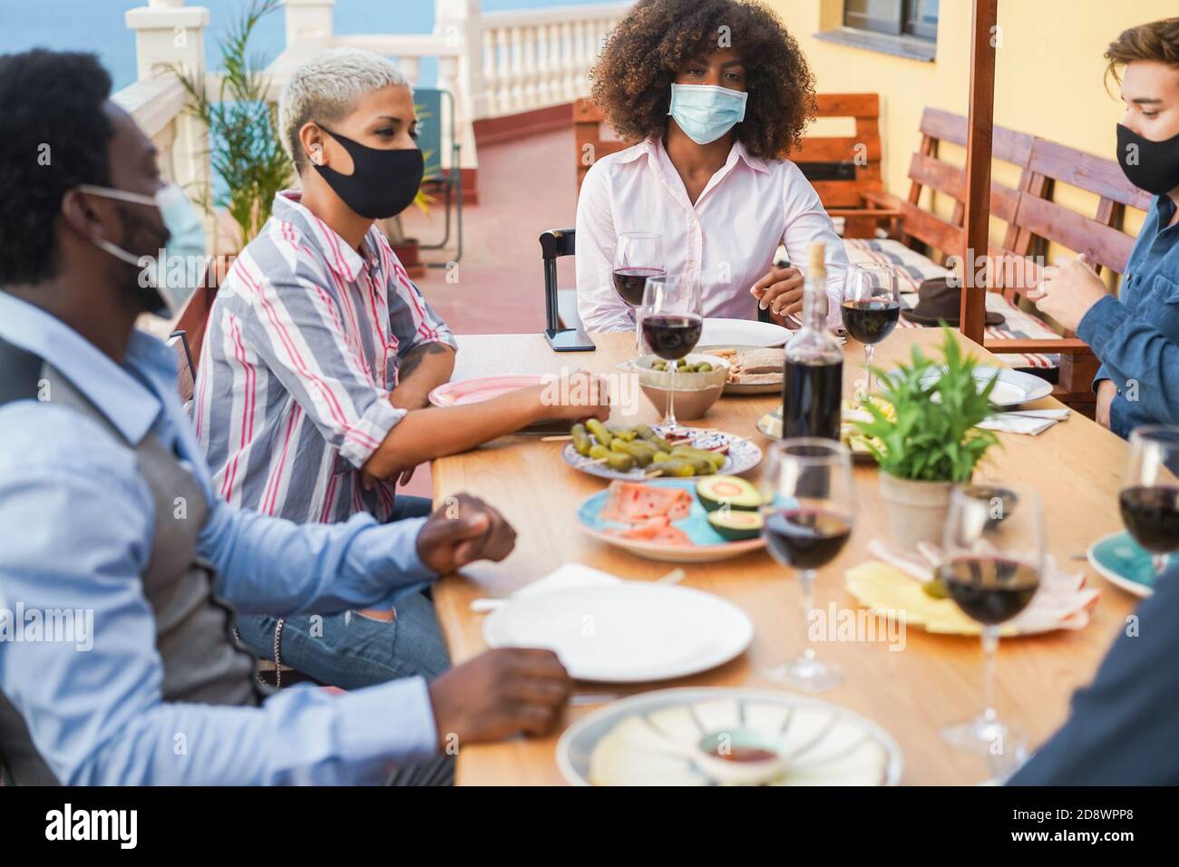 Young multiracial people eating and drinking together while wearing ...