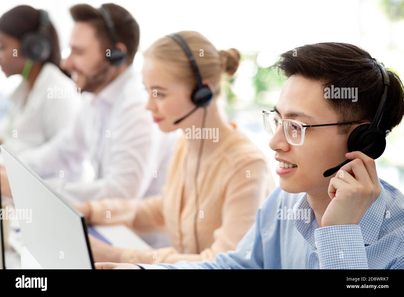 Asian hotline operator and his colleagues working at modern call centre ...