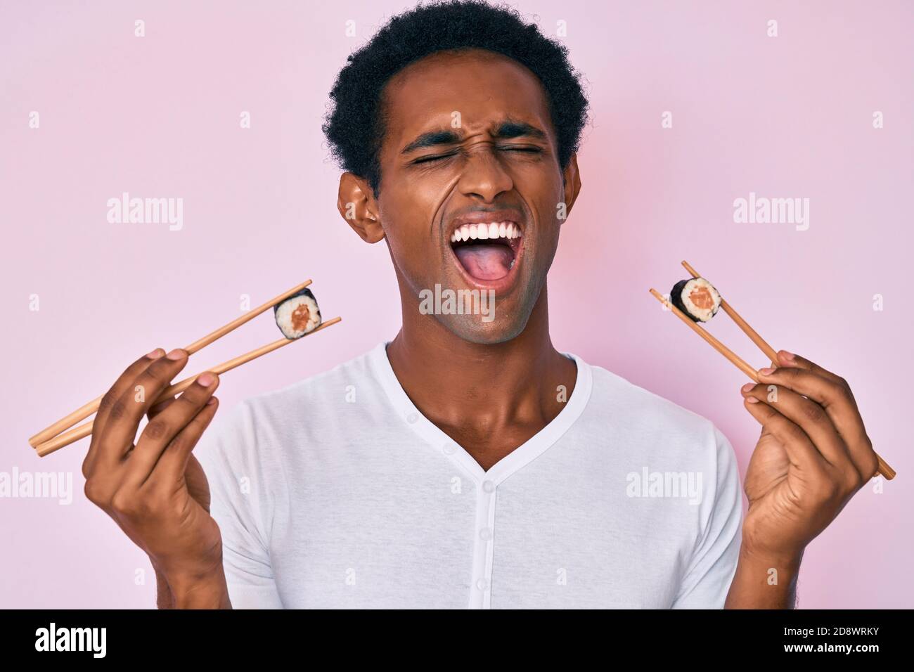 African handsome man eating sushi using chopsticks angry and mad ...