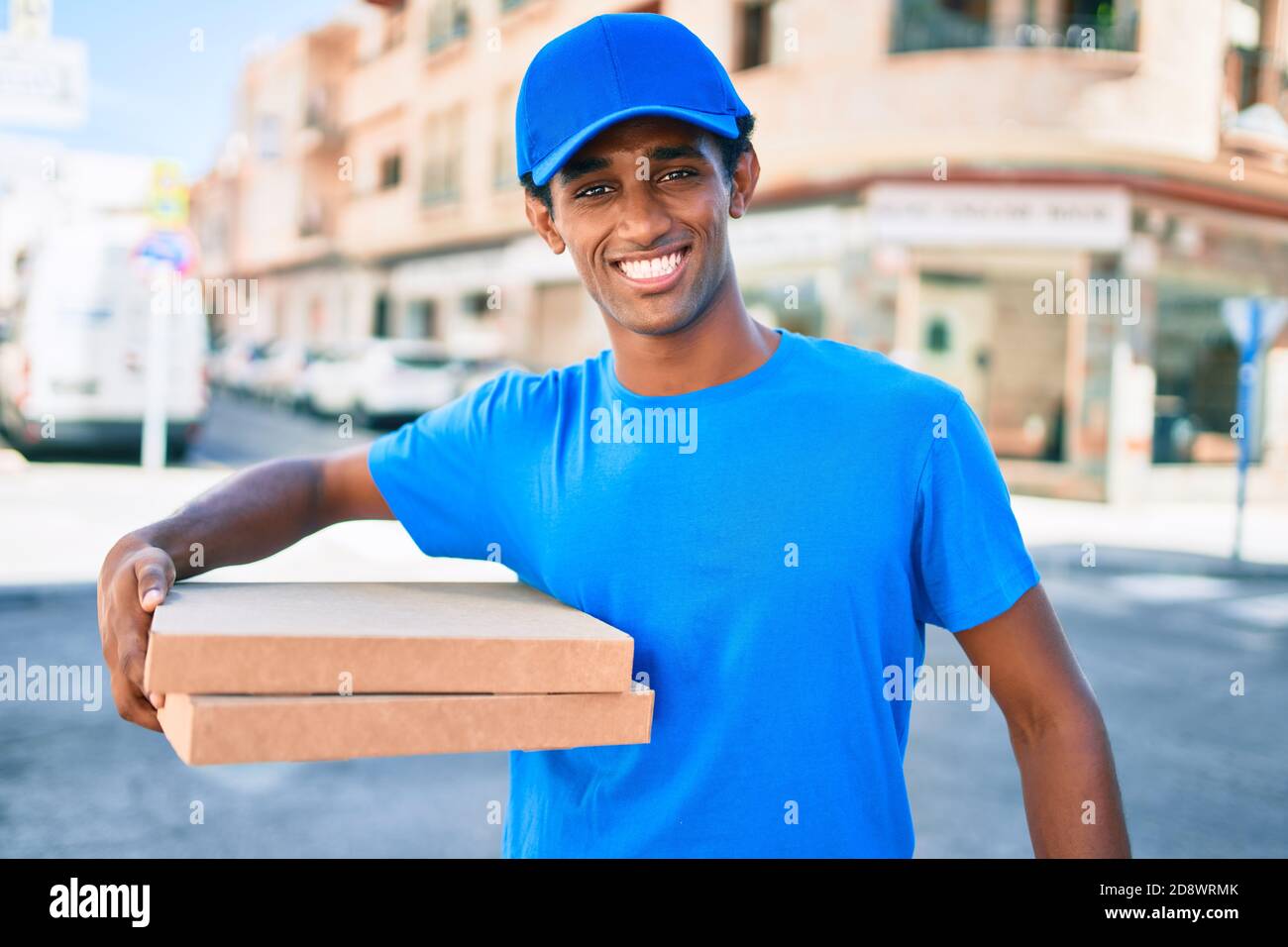 African delivery man wearing courier uniform outdoors holding take away ...