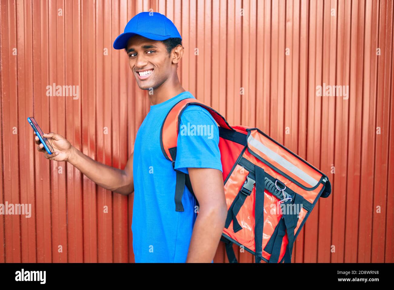 African delivery man wearing courier uniform outdoors using smartphone ...