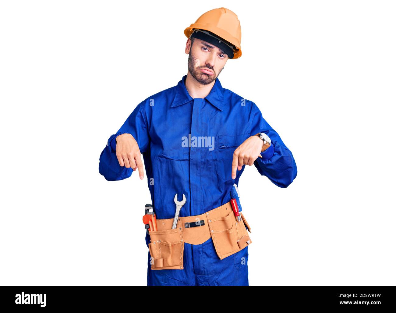 Young hispanic man wearing worker uniform pointing down looking sad and ...