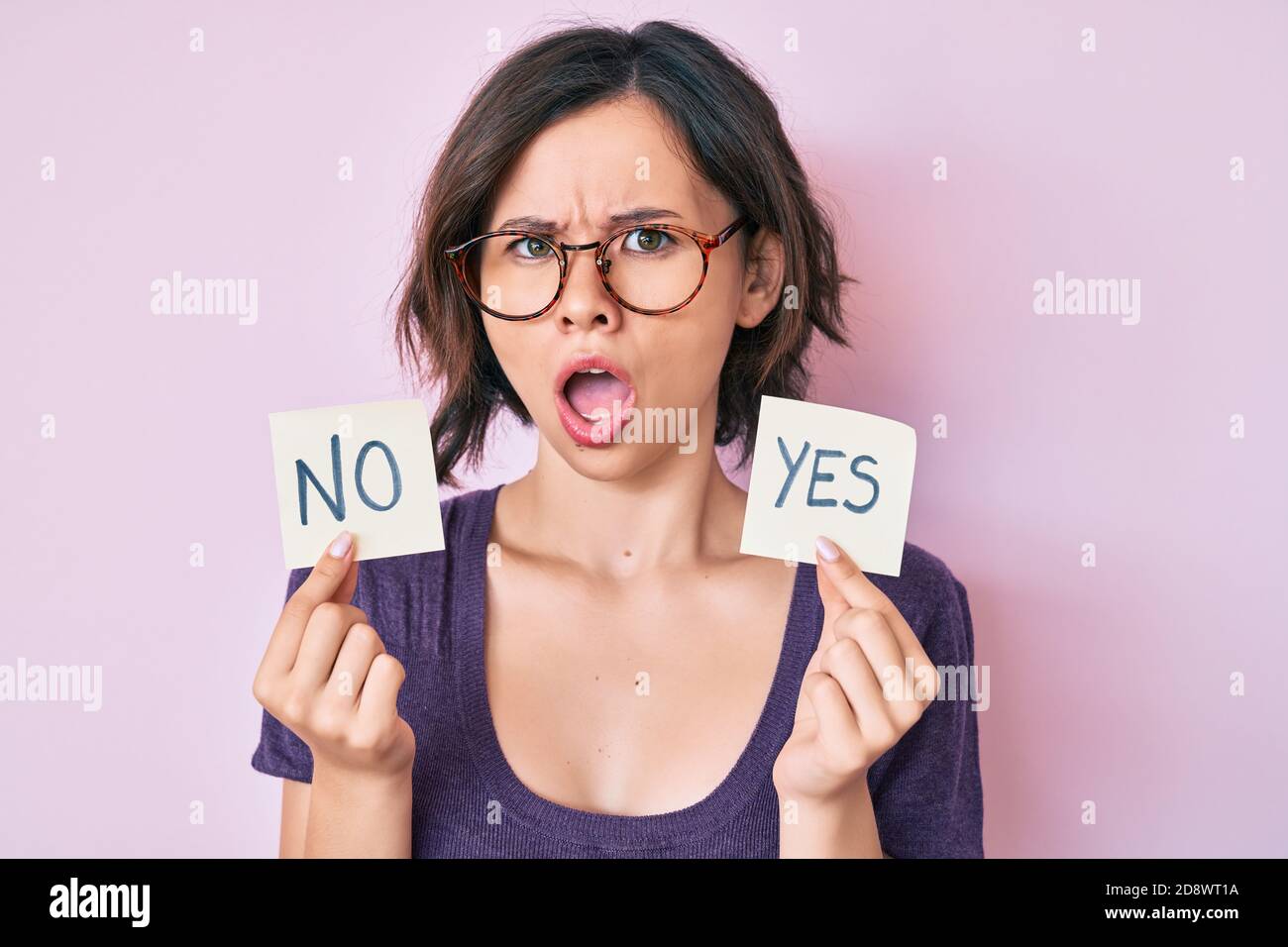 Young beautiful girl holding yes and no reminder in shock face, looking ...