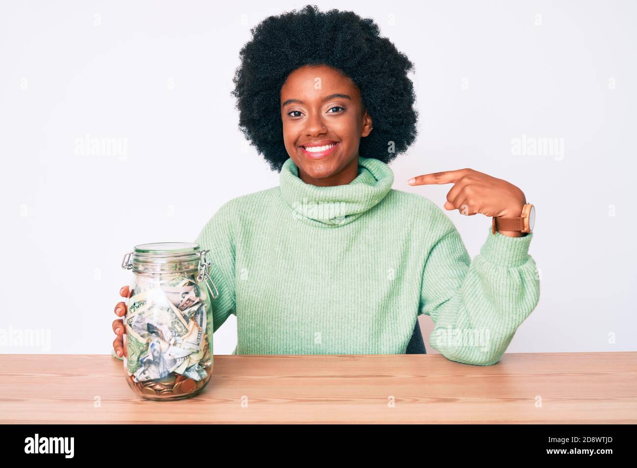 Young african american woman holding jar with savings pointing finger ...