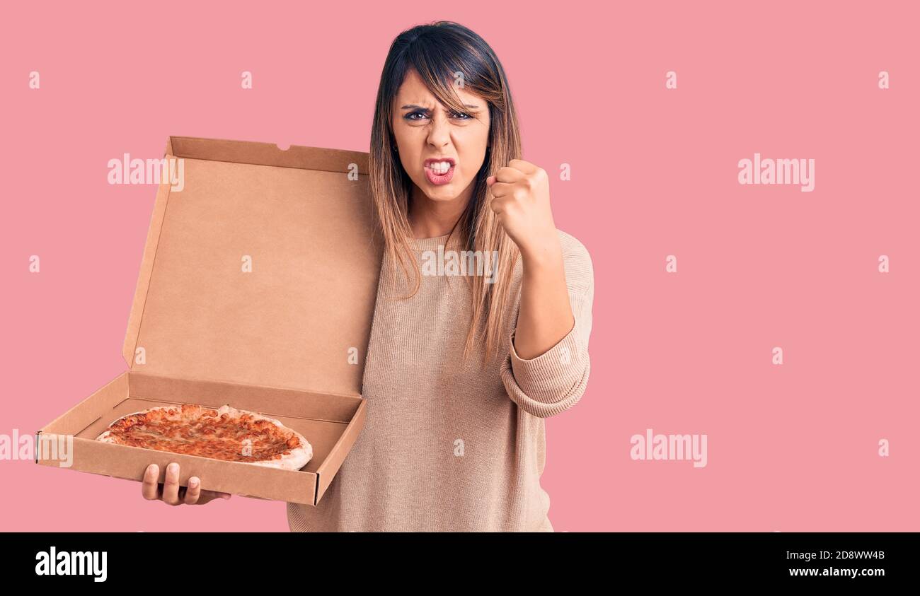 Young beautiful woman holding delivery cardboard box with pizza annoyed ...