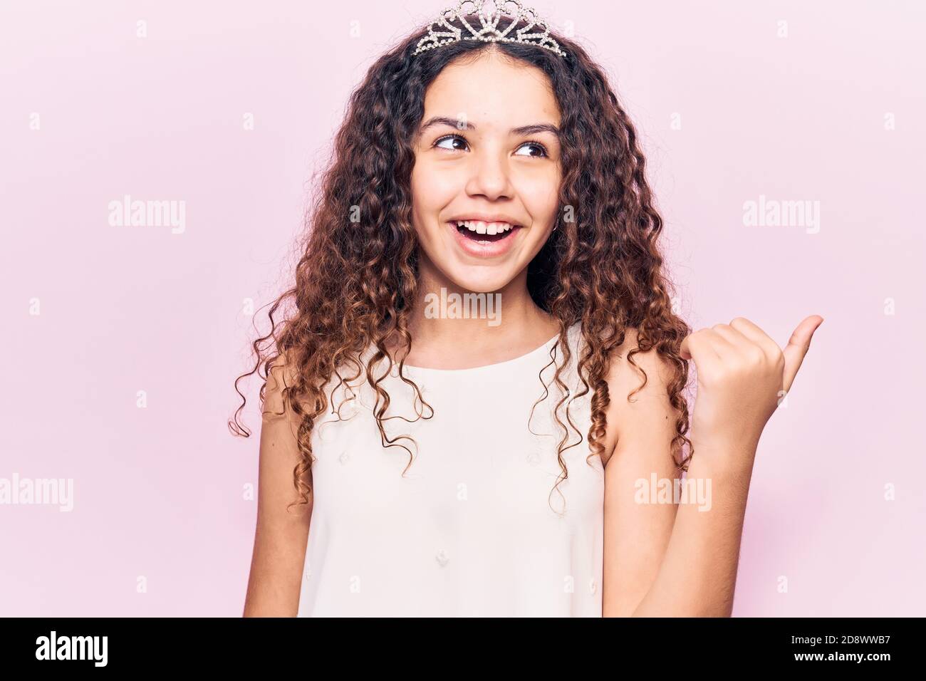 Beautiful kid girl with curly hair wearing princess tiara pointing ...