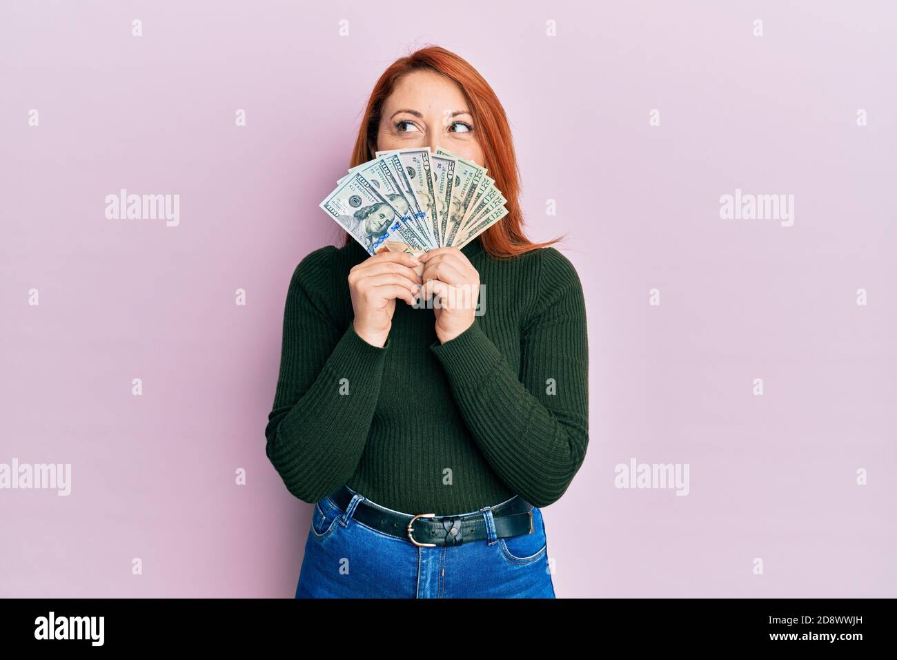 Beautiful redhead woman holding dollars close to face smiling looking ...