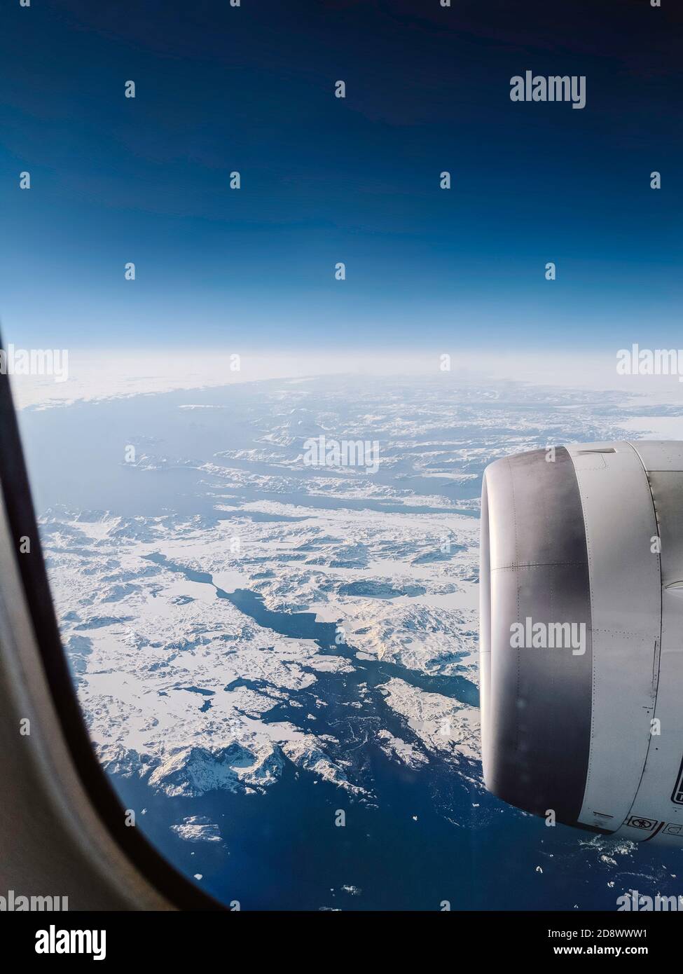 A view from a plane window on sky and arctic Greenland and Ocean. Snow ...