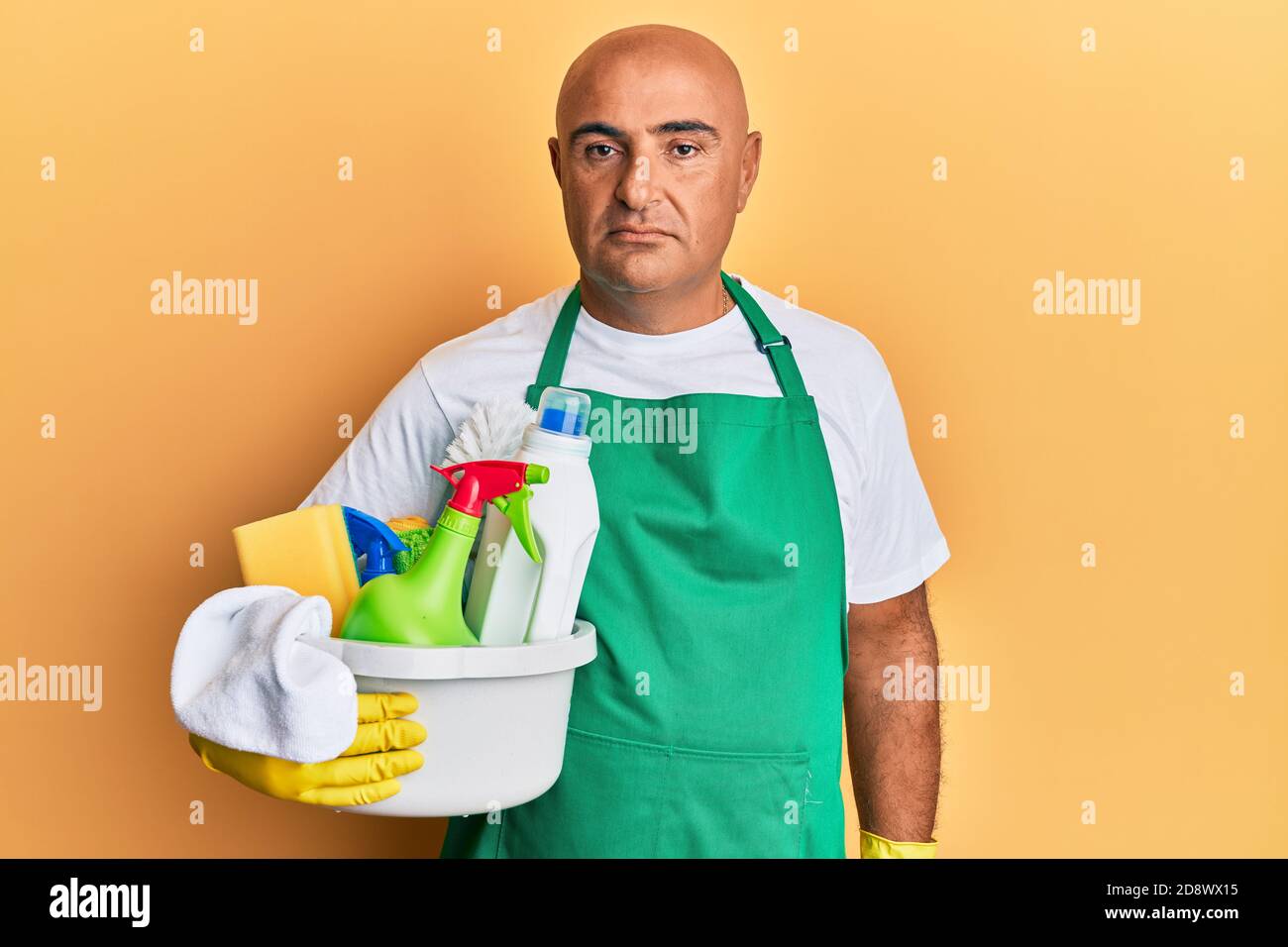 Mature middle east man wearing cleaner apron holding cleaning products ...