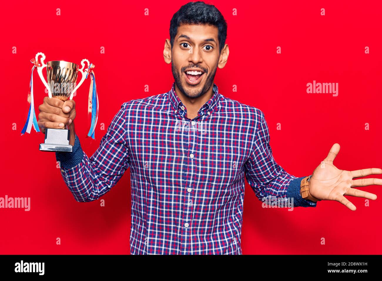 Young latin man holding winner trophy celebrating achievement with ...