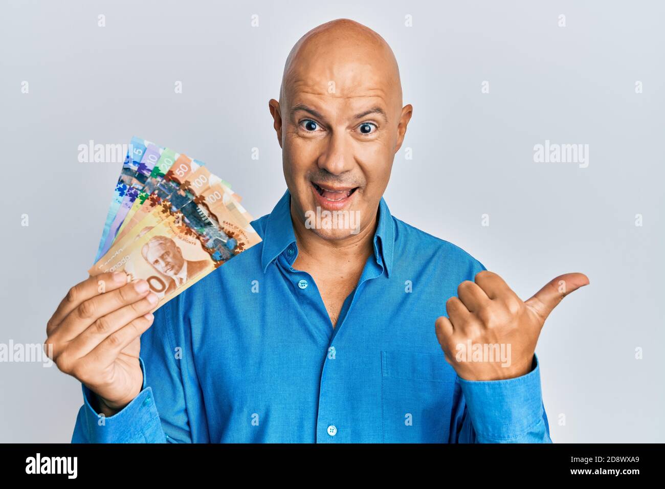 Middle age bald man holding canadian dollars pointing thumb up to the ...
