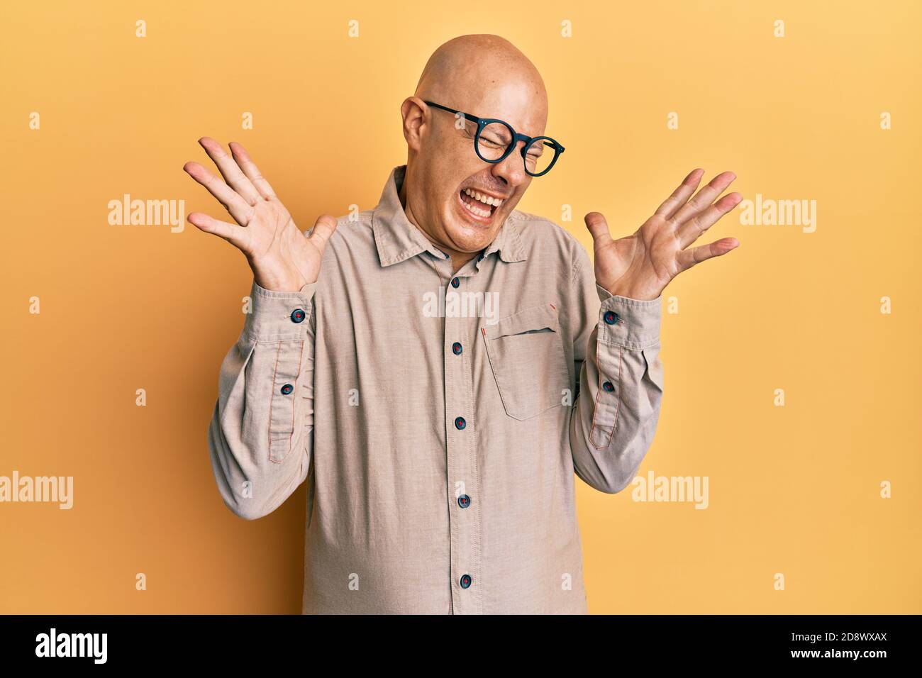 Middle age bald man wearing casual clothes and glasses celebrating mad ...