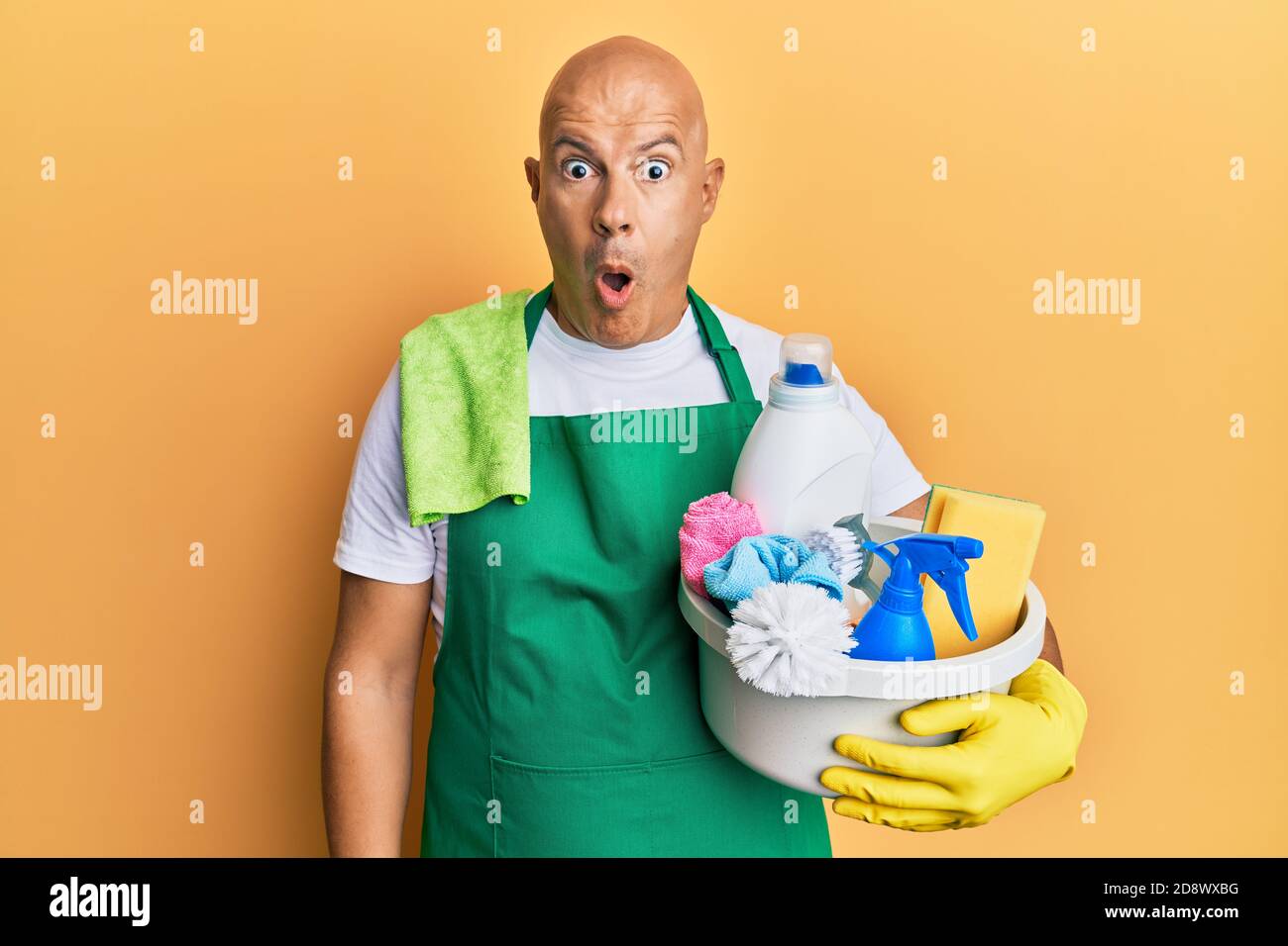 Middle age bald man wearing cleaner apron holding cleaning products ...