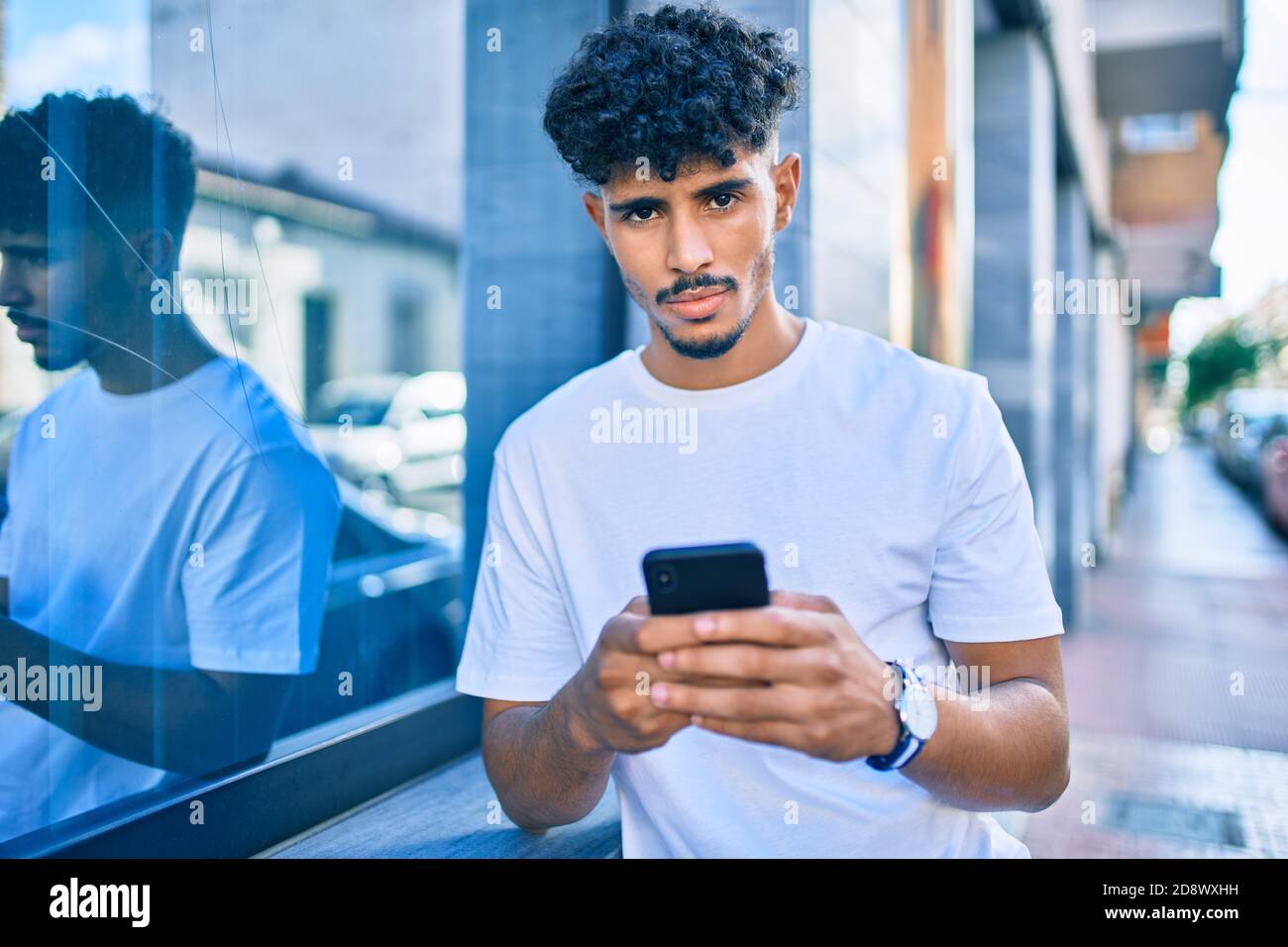 Young arab man with serious expression using smartphone leaning on the ...