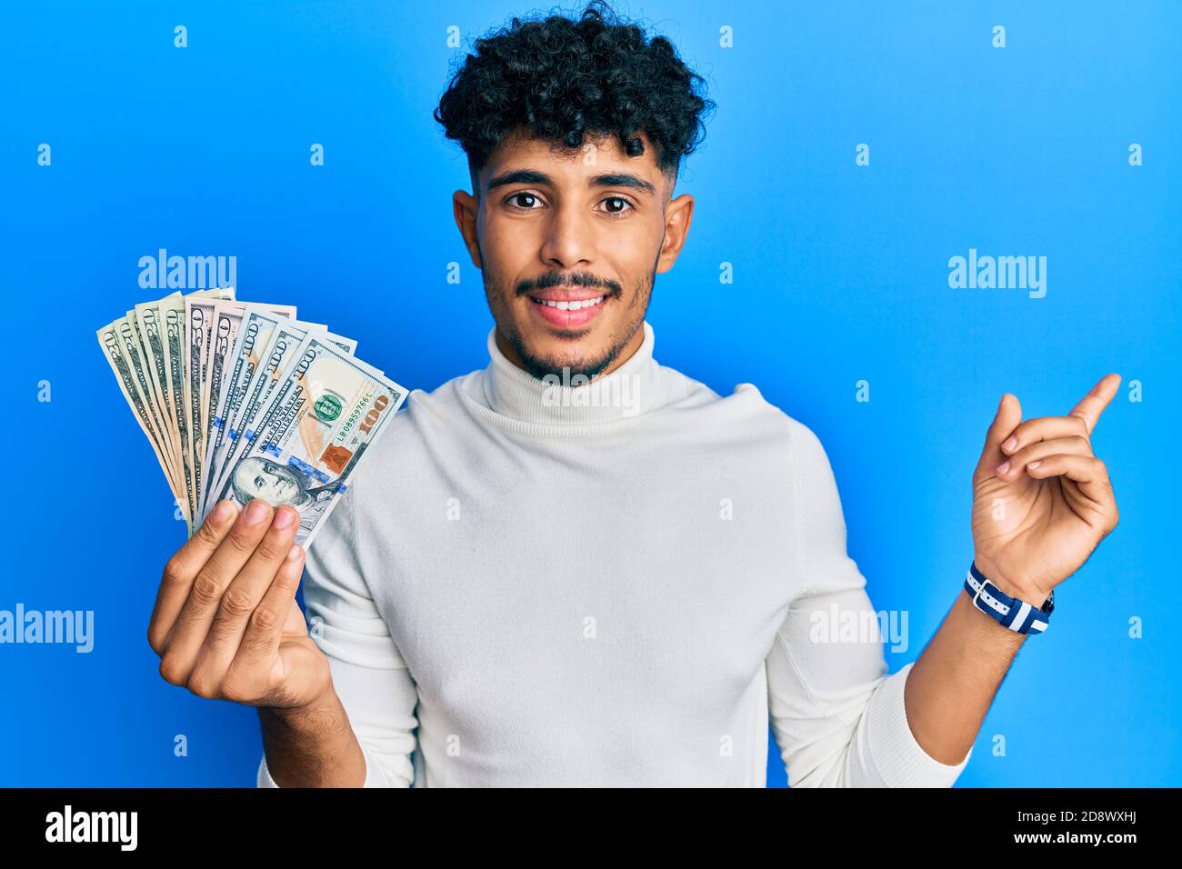 Young arab handsome man holding dollars smiling happy pointing with ...