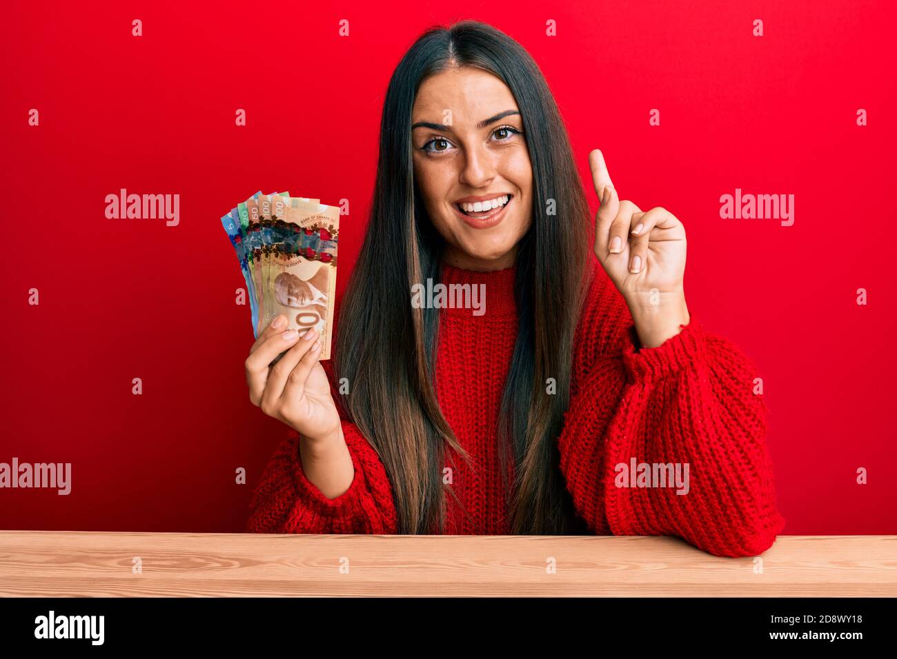 Beautiful hispanic woman holding canadian dollars smiling with an idea ...
