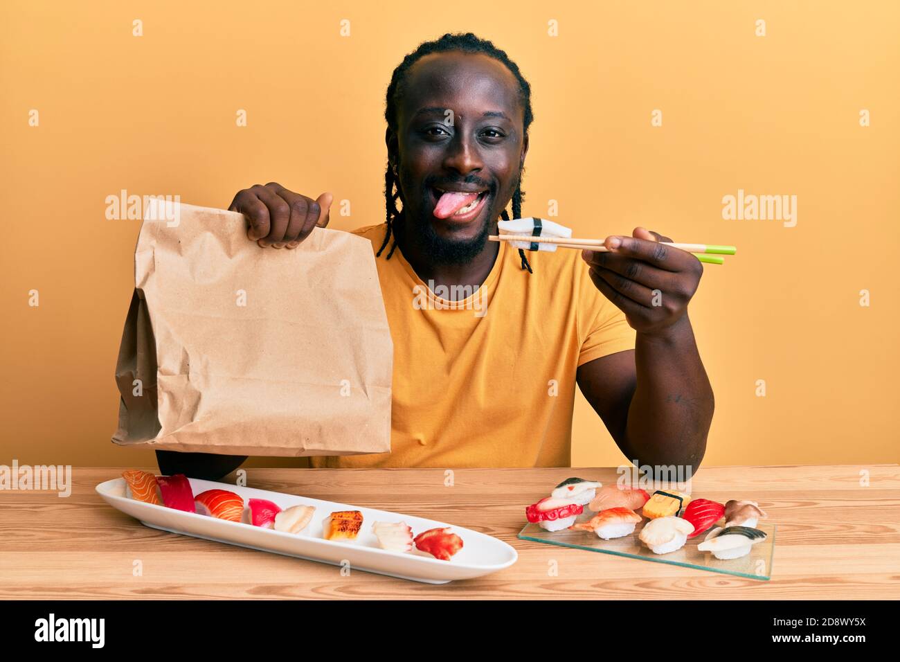 Handsome Young Black Man Eating Take Away Sushi Sitting On The Table