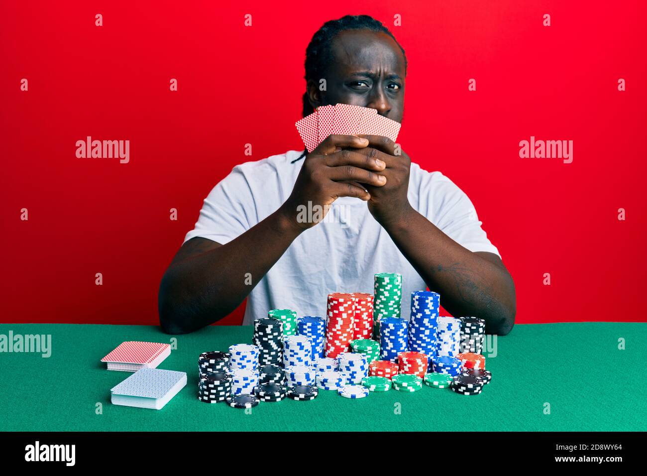 Handsome young black man playing gambling poker covering face with ...