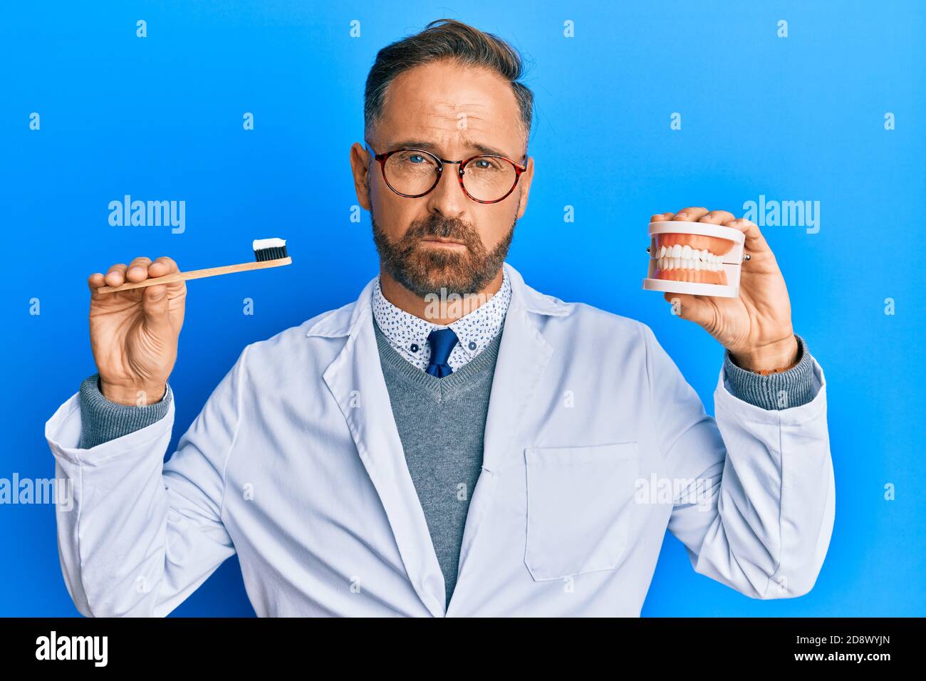 Handsome middle age dentist man holding denture and toothbrush ...