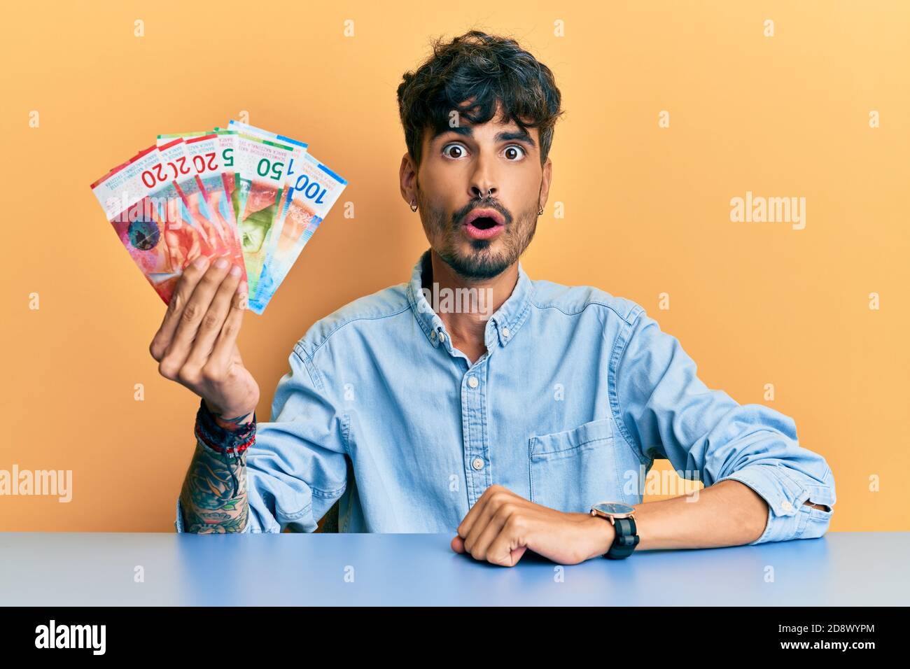 Young hispanic man holding swiss franc banknotes sitting on the table ...