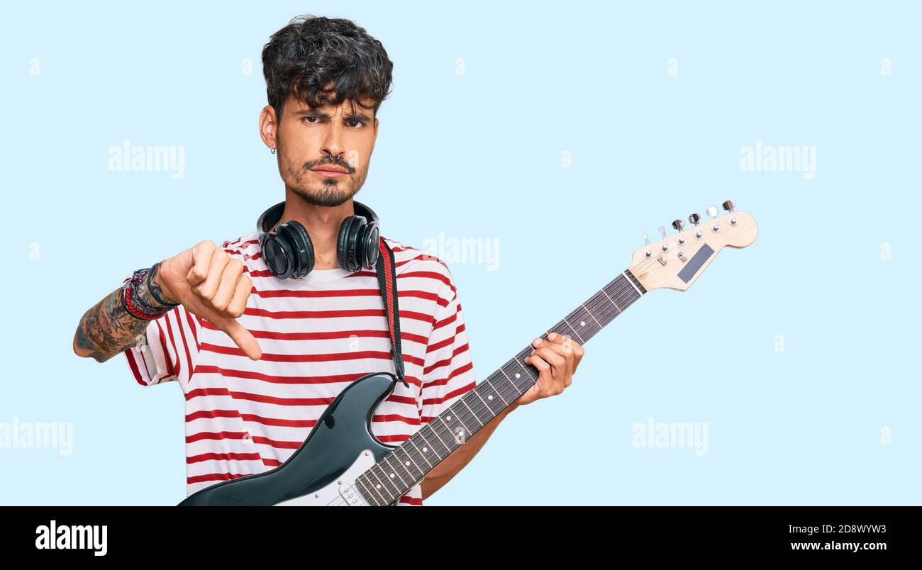 Young hispanic man playing electric guitar with angry face, negative ...