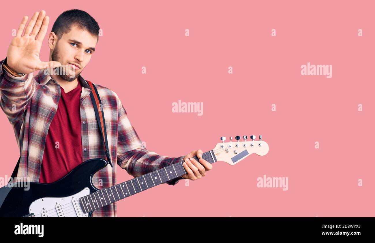 Young handsome man playing electric guitar with open hand doing stop ...